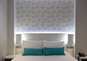 Quarto de hotel com cama, duas almofadas, mesa de cabeceira, telefone e parede com padrão floral.