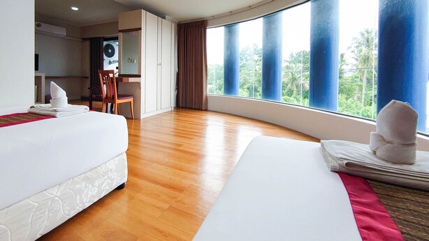 Quarto de hotel com duas camas, piso de madeira, uma janela grande com vista e uma pequena escrivaninha com cadeira.