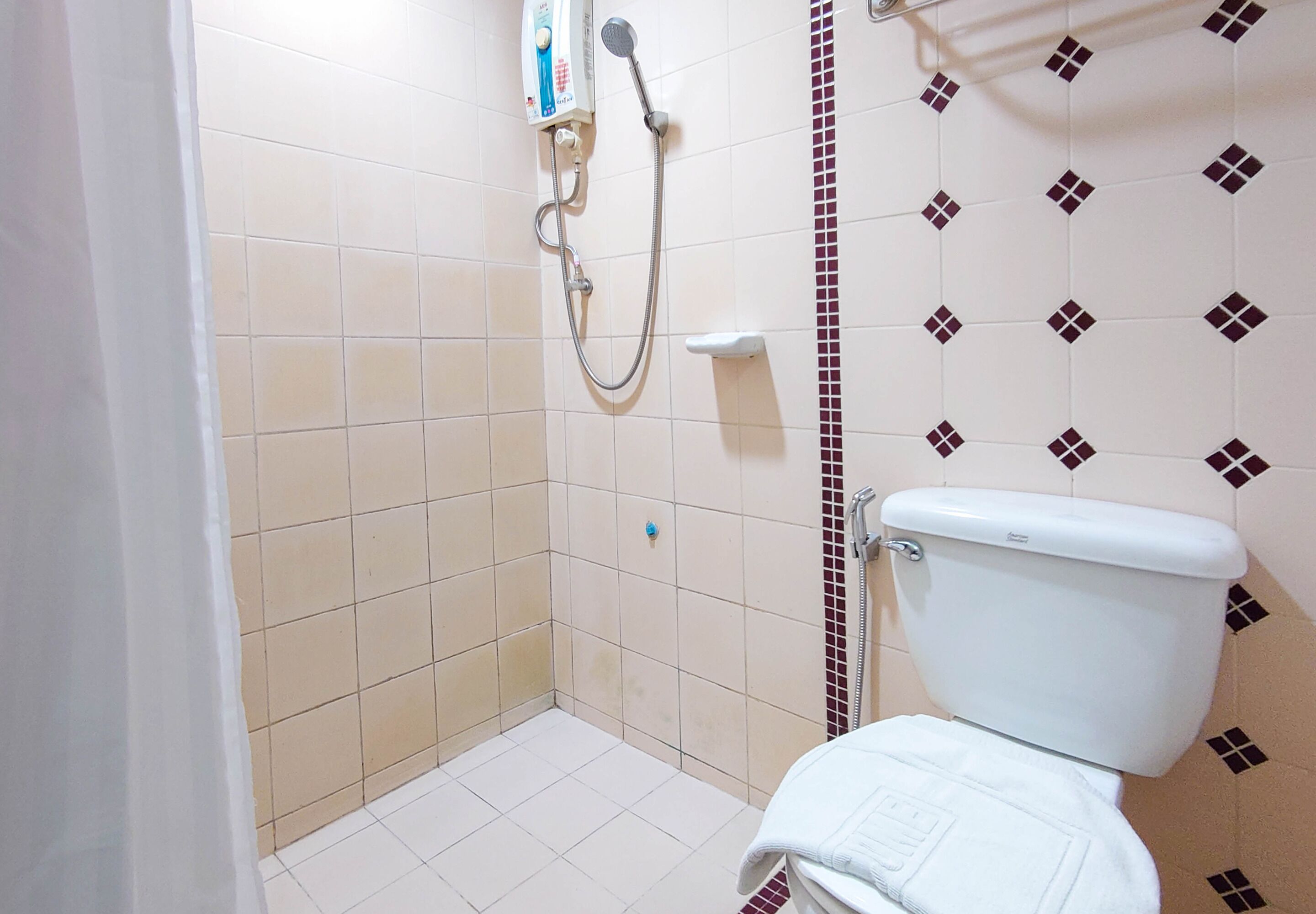 Uma casa de banho com chuveiro, sanita e paredes revestidas a azulejos.