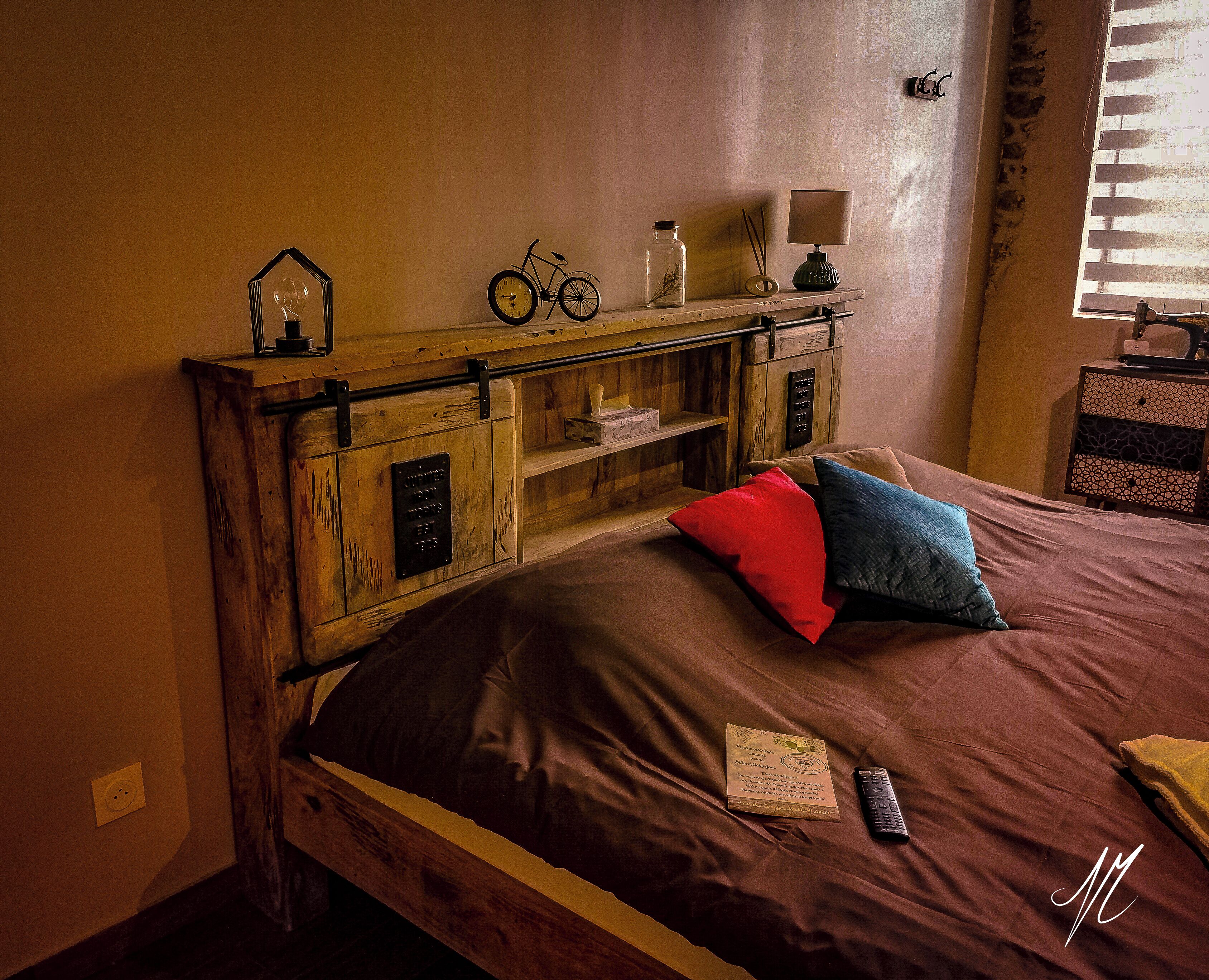 Uma cama com cabeceira de madeira, um controle remoto e um livro sobre a cama.