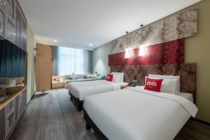 Quarto de hotel com duas camas, televisão, escrivaninha e área de estar com vista para a cidade.