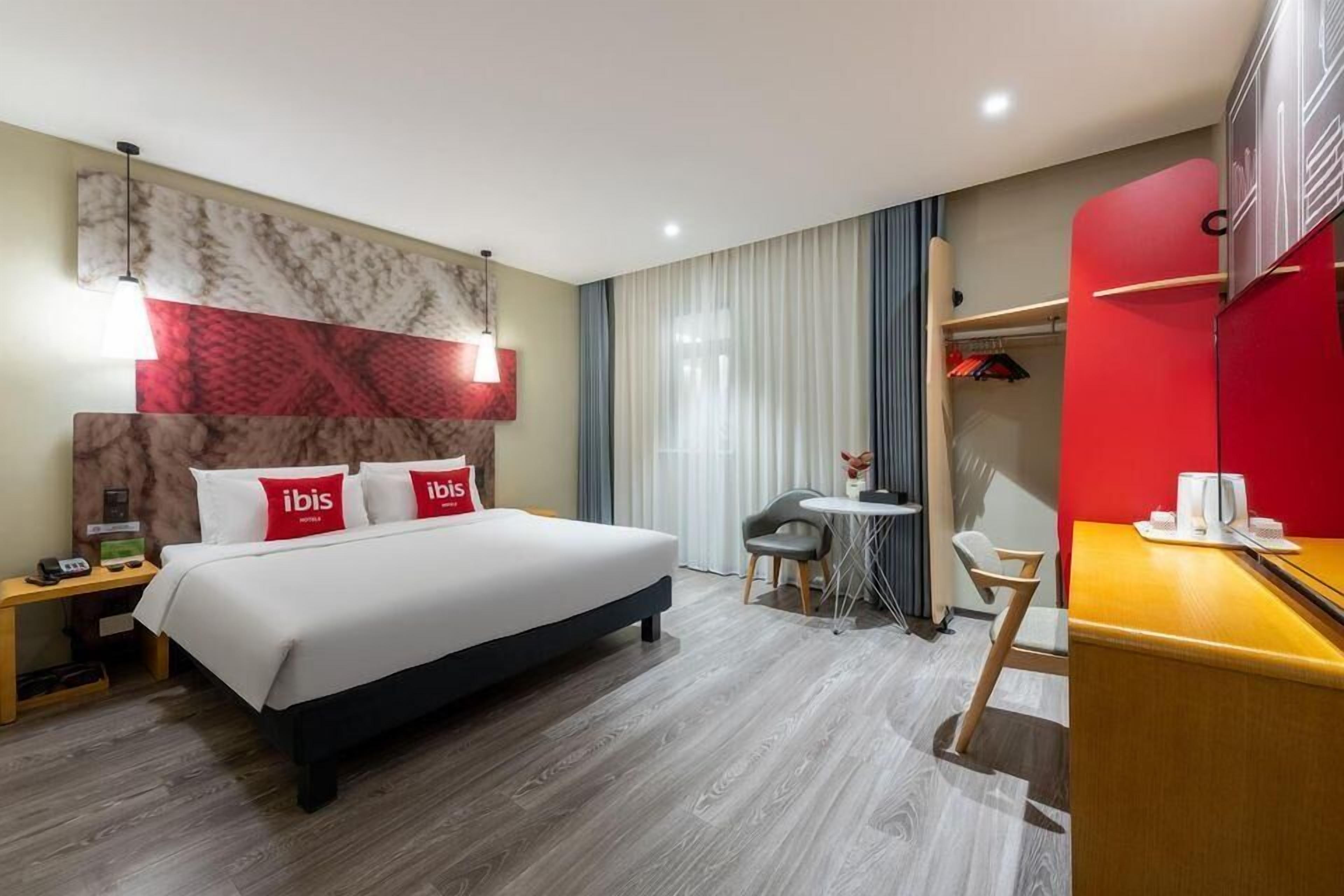Quarto de hotel com cama, mesas de cabeceira, escrivaninha e uma cadeira.