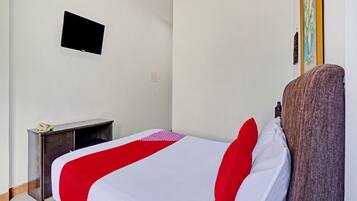Quarto de hotel com cama, escrivaninha, cadeira, televisão e um quadro na parede.