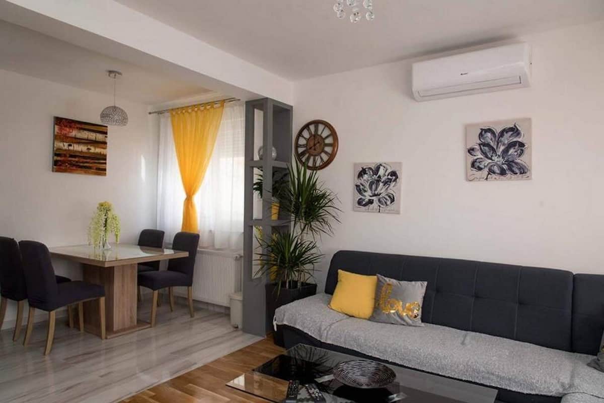 Uma sala de estar moderna com um sofá cinza escuro, uma mesa de centro de vidro e um espaço de jantar com mesa e cadeiras de madeira.
