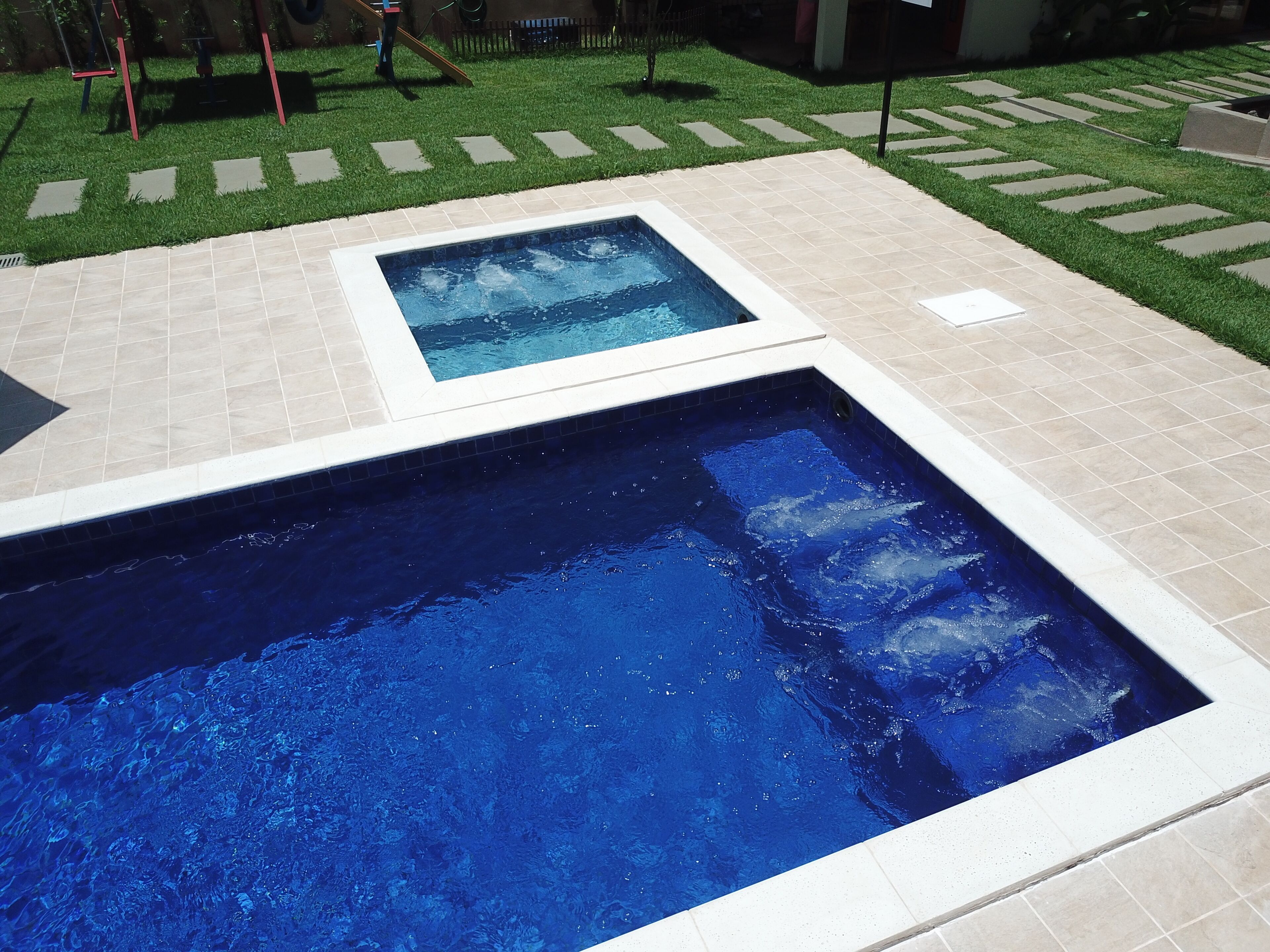 Uma piscina retangular com borda em azulejo, rodeada por um espaço de pátio com um caminho decorado.