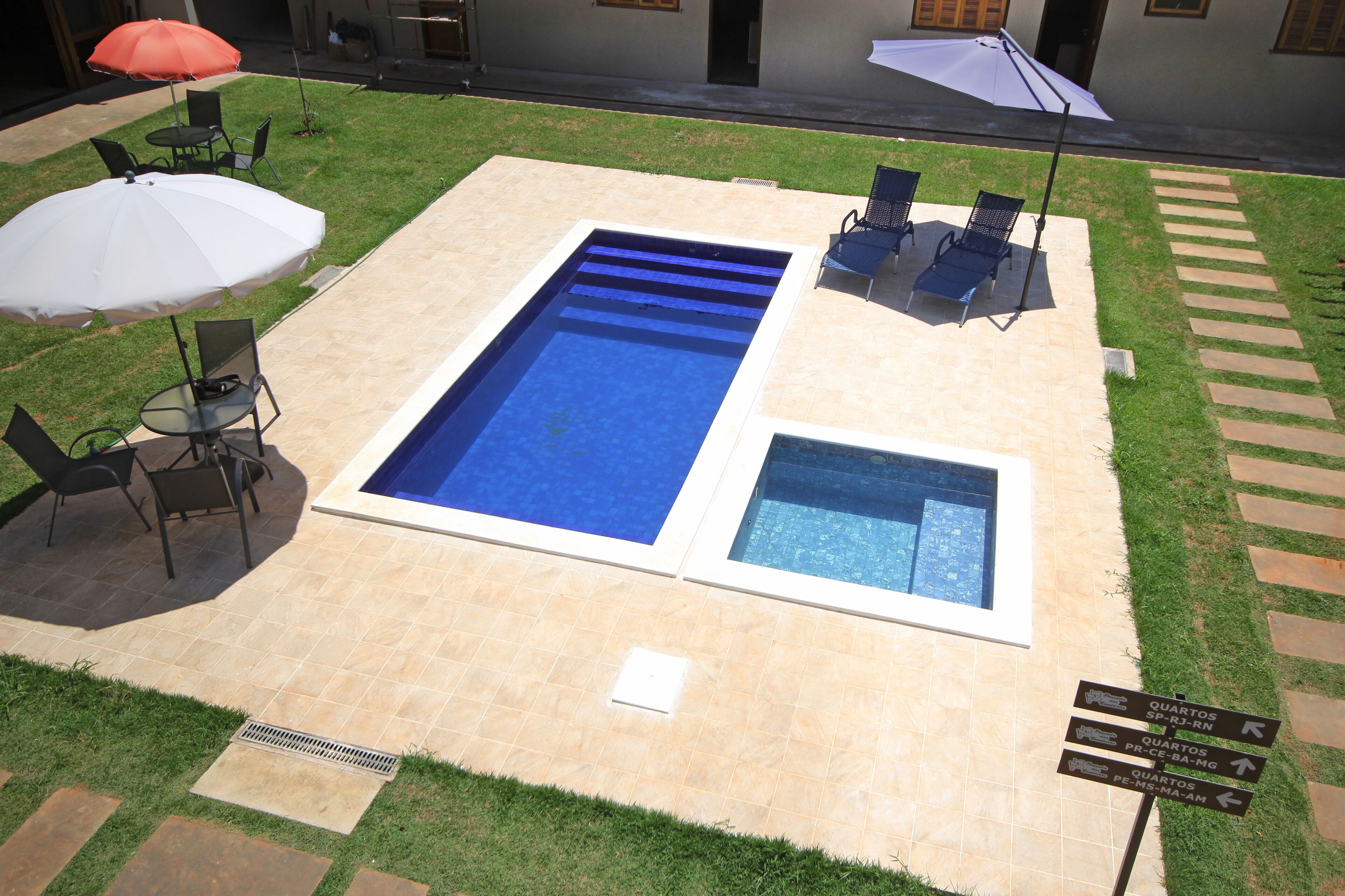 Piscina com duas áreas distintas, rodeada por um espaço de pátio com cadeiras e guarda-sóis.