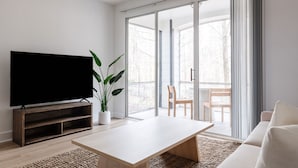 Uma sala de estar moderna com televisão de tela plana, uma mesa de centro, um vaso com planta e uma porta de vidro deslizante que dá para uma área externa com uma cadeira.