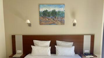Uma cama grande com lençóis brancos, cabeceira de madeira, duas mesas de cabeceira com abajures e um quadro na parede.