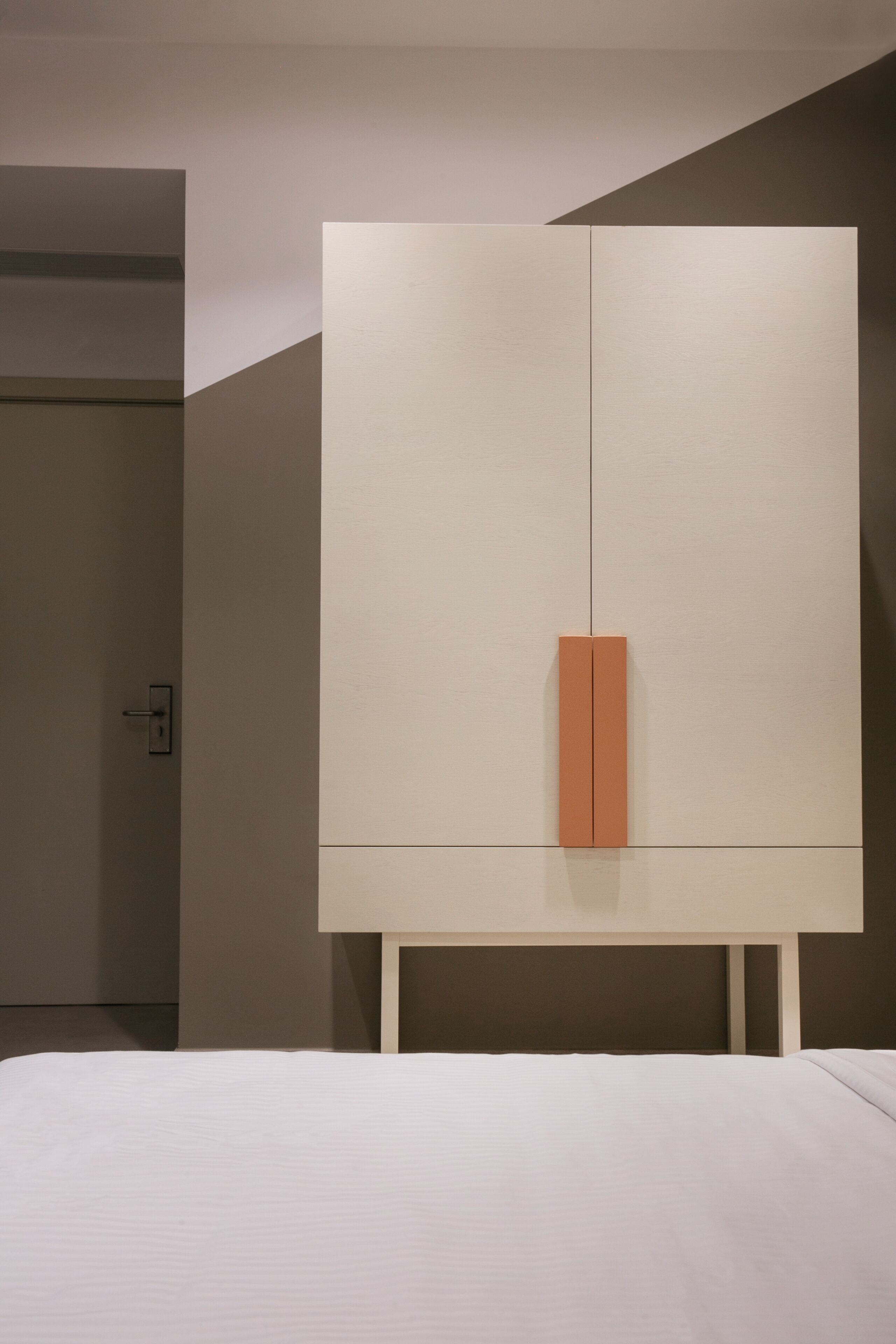 Quarto minimalista com uma cama, um guarda-roupa espaçoso e uma porta.