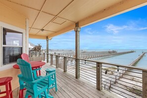 Um deck de madeira com mesa e cadeiras, com vista para uma praia e um píer.