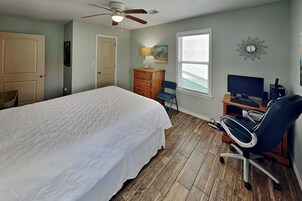 Quarto com uma cama, uma escrivaninha com computador, uma cadeira, abajur e ventoinha de teto.