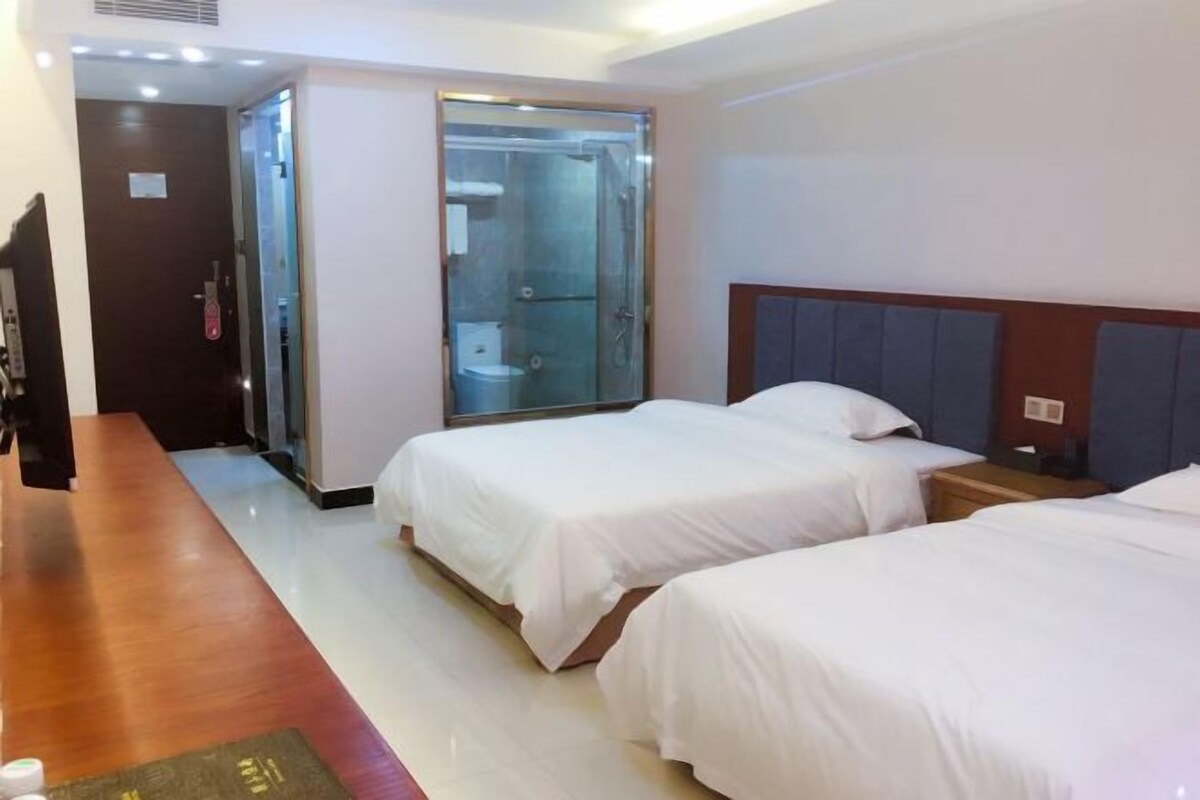 Quarto de hotel com duas camas, piso de madeira, chuveiro com divisória de vidro e cabeceira de madeira.