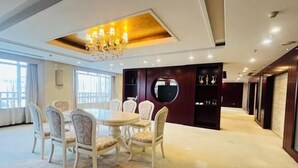 Um quarto amplo com uma mesa de jantar redonda, cadeiras estofadas brancas, um candelabro e uma grande janela.