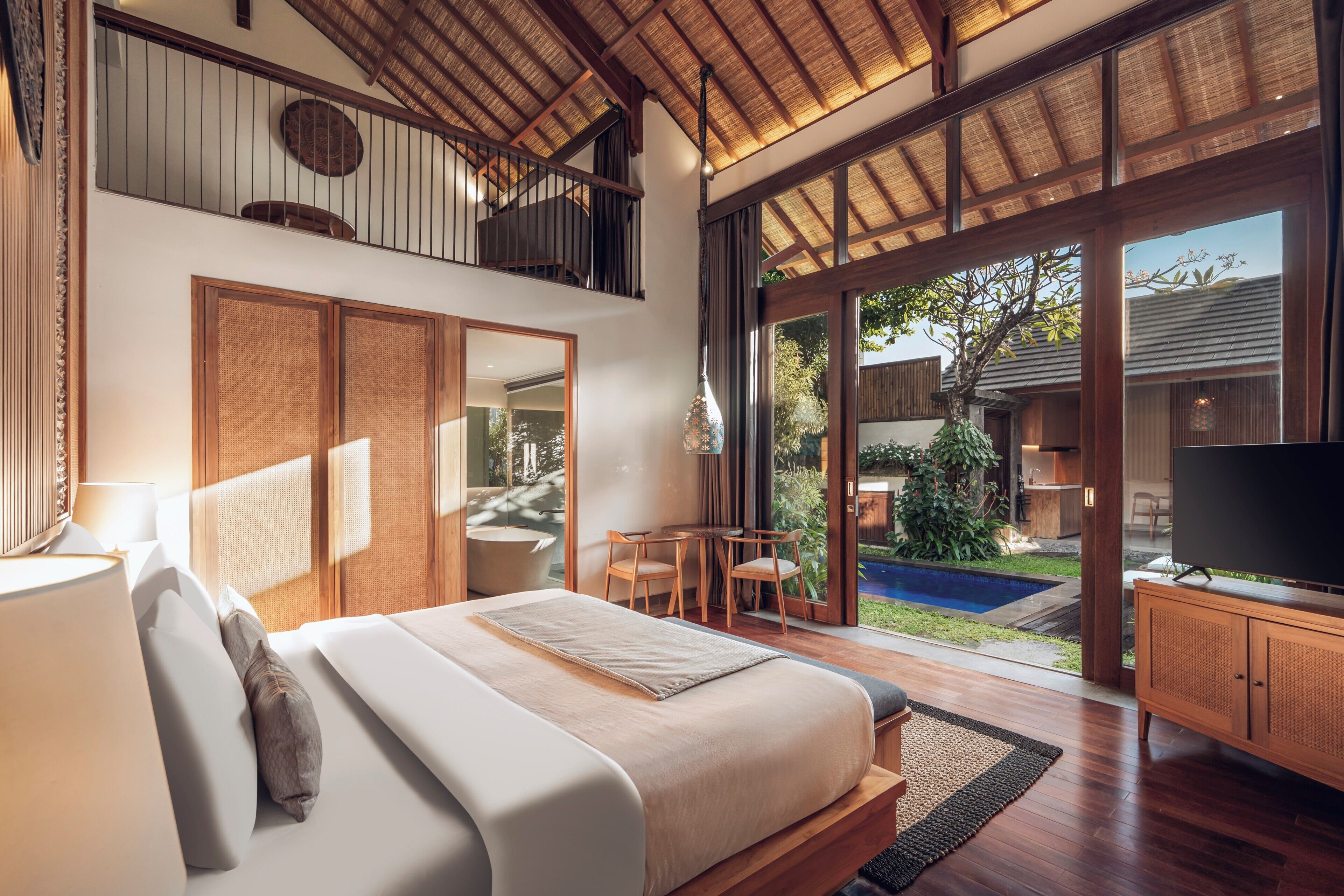 Quarto com cama, televisão, varanda com piscina e área de jantar.