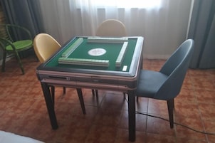 Quarto com mesa e cadeiras de azulejos, janela com cortinas e piso ladrilhado.