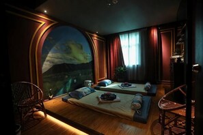 Quarto com uma grande janela em arco, duas camas, uma cadeira e uma mesinha com bandeja.
