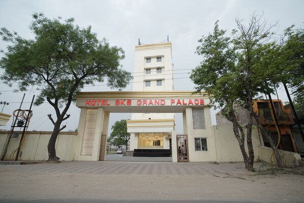 A entrada do Hotel S.K.S Grand Palace, com vista clara para a entrada principal e um edifício alto ao fundo.