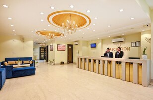 Uma área de recepção com balcão, dois recepcionistas, um sofá azul e um lustre.