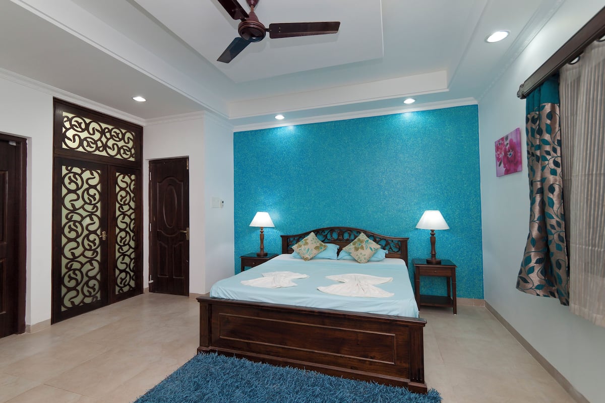 Quarto com cama, duas mesas de cabeceira com abajures, ventilador de teto e parede azul com textura.