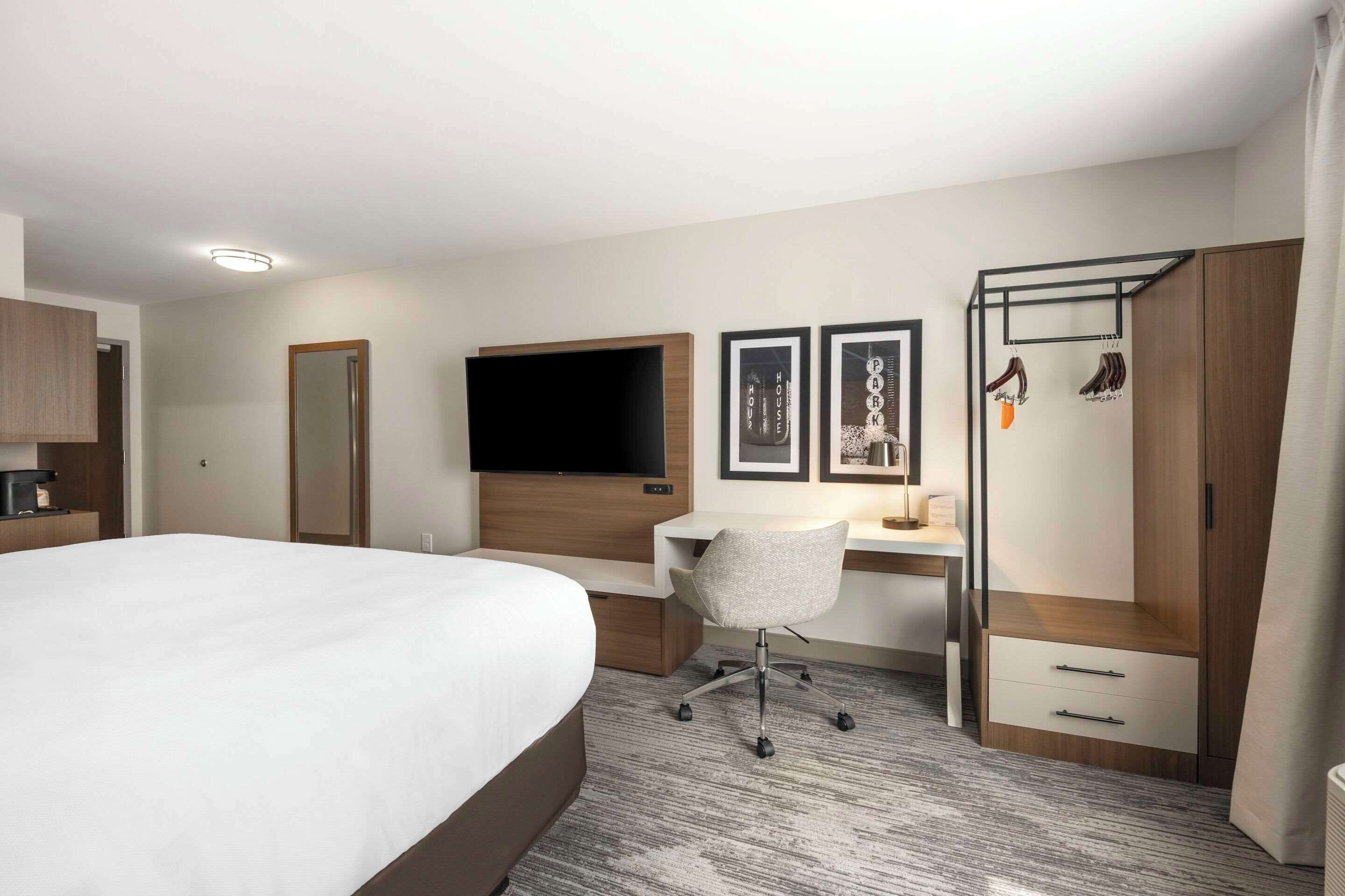 Quarto de hotel com uma cama grande, uma escrivaninha com cadeira, televisão e guarda-roupa.