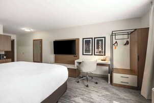 Quarto de hotel com uma cama grande, uma escrivaninha com cadeira, televisão e guarda-roupa.