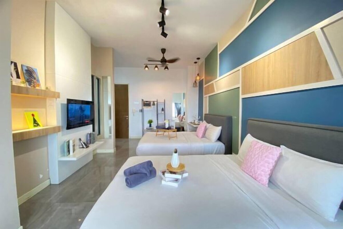 Quarto de hotel moderno com uma cama grande, televisão, ventoinha no teto e um pequeno espaço de estar com mesa e cadeiras.