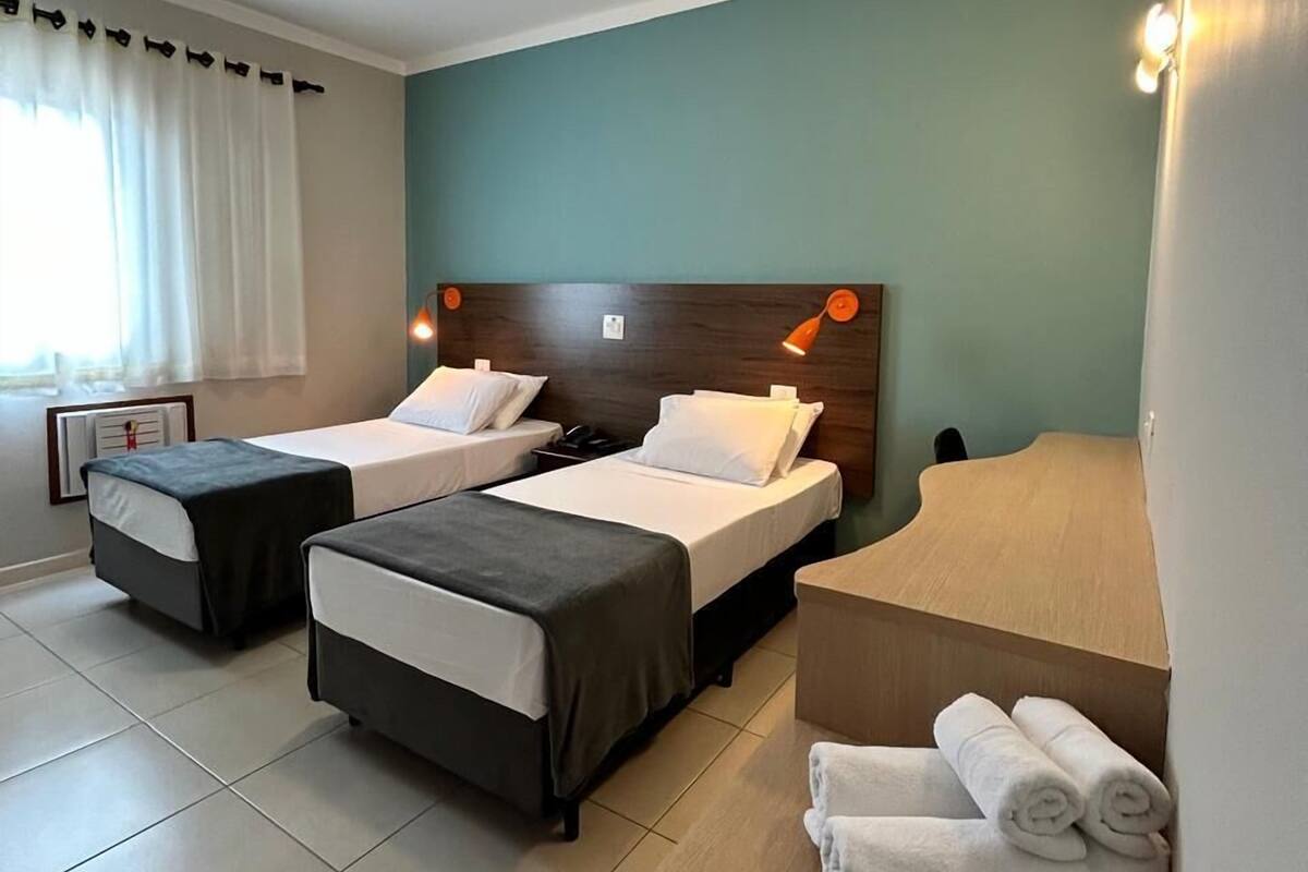 Quarto de hotel com duas camas, uma escrivaninha e uma cadeira.