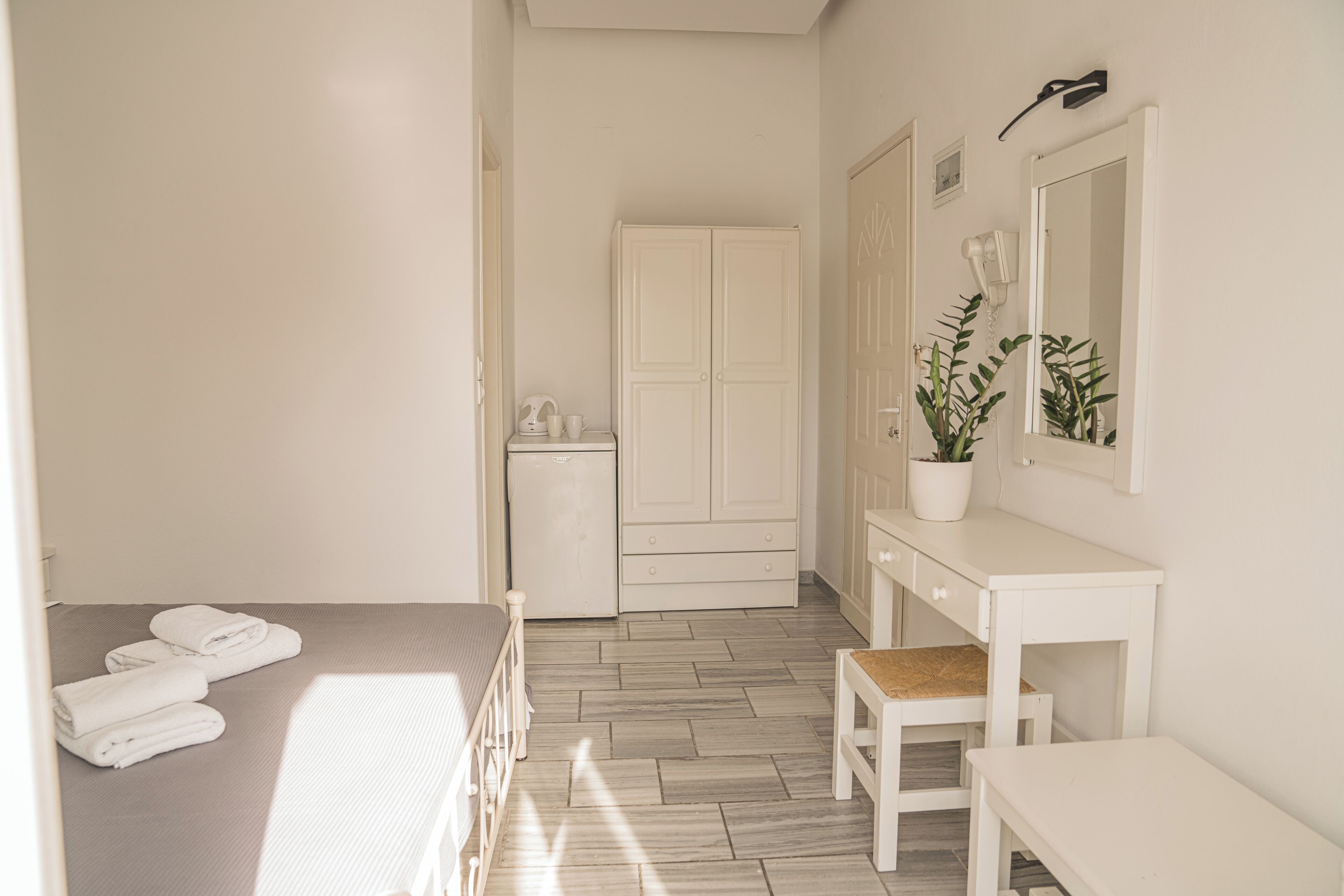 Quarto pequeno e limpo com cama, escrivaninha, espelho e planta em vaso.
