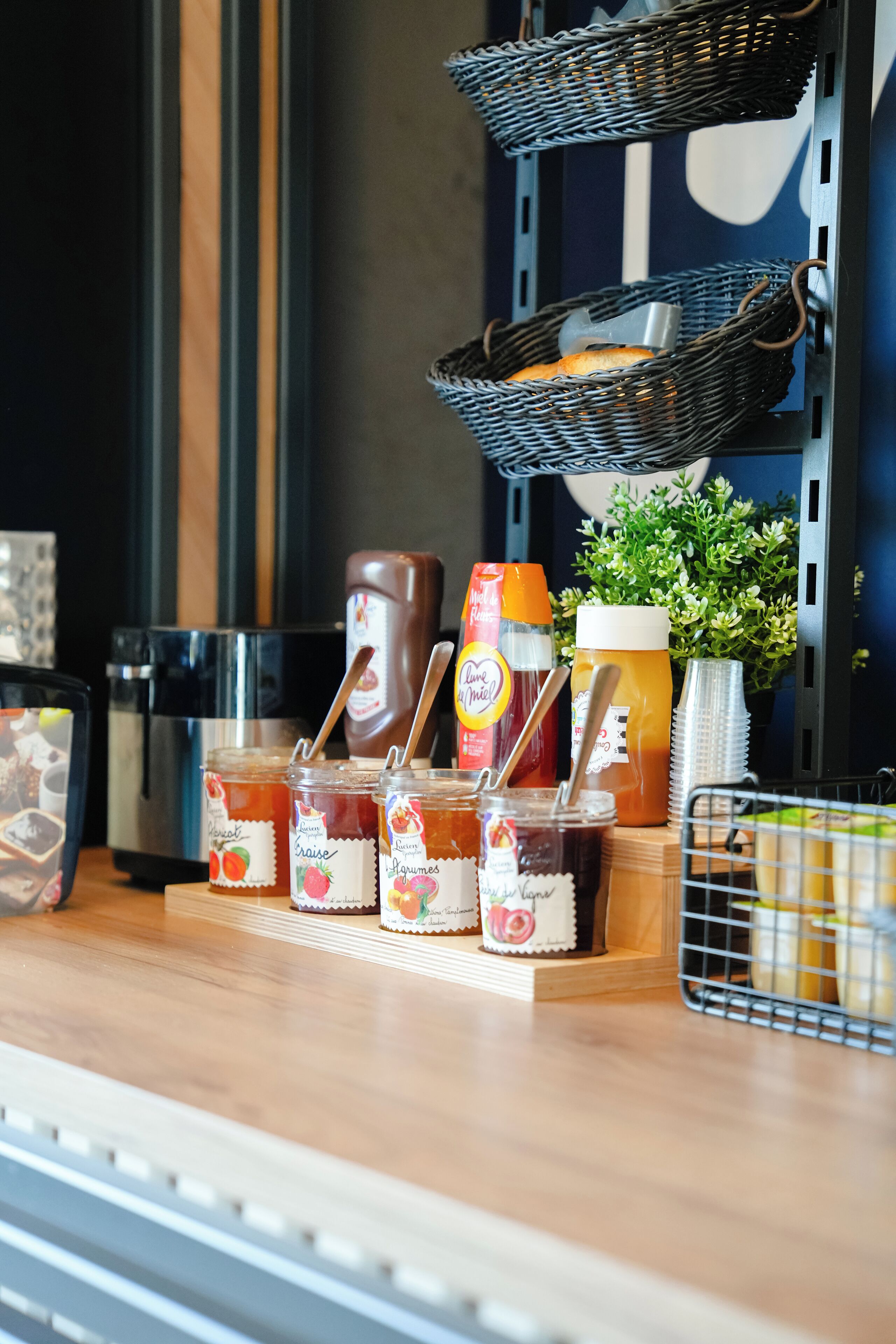 Uma bancada de cozinha com diversos alimentos, incluindo potes de compota, um frasco de ketchup e uma cesta com pão.