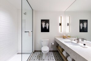 Uma casa de banho moderna com cabine de duche em vidro, sanita branca e lavatório de mármore com um espelho grande.