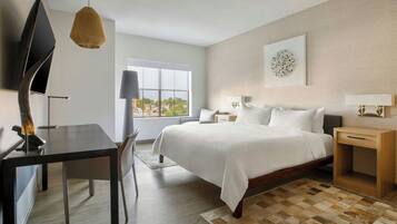 Quarto de hotel moderno com cama, mesas de cabeceira, escrivaninha e televisão.