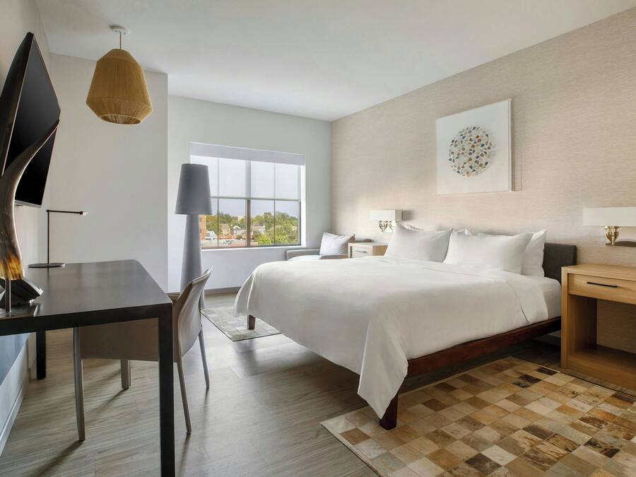 Quarto de hotel moderno com cama, mesas de cabeceira, escrivaninha e televisão.