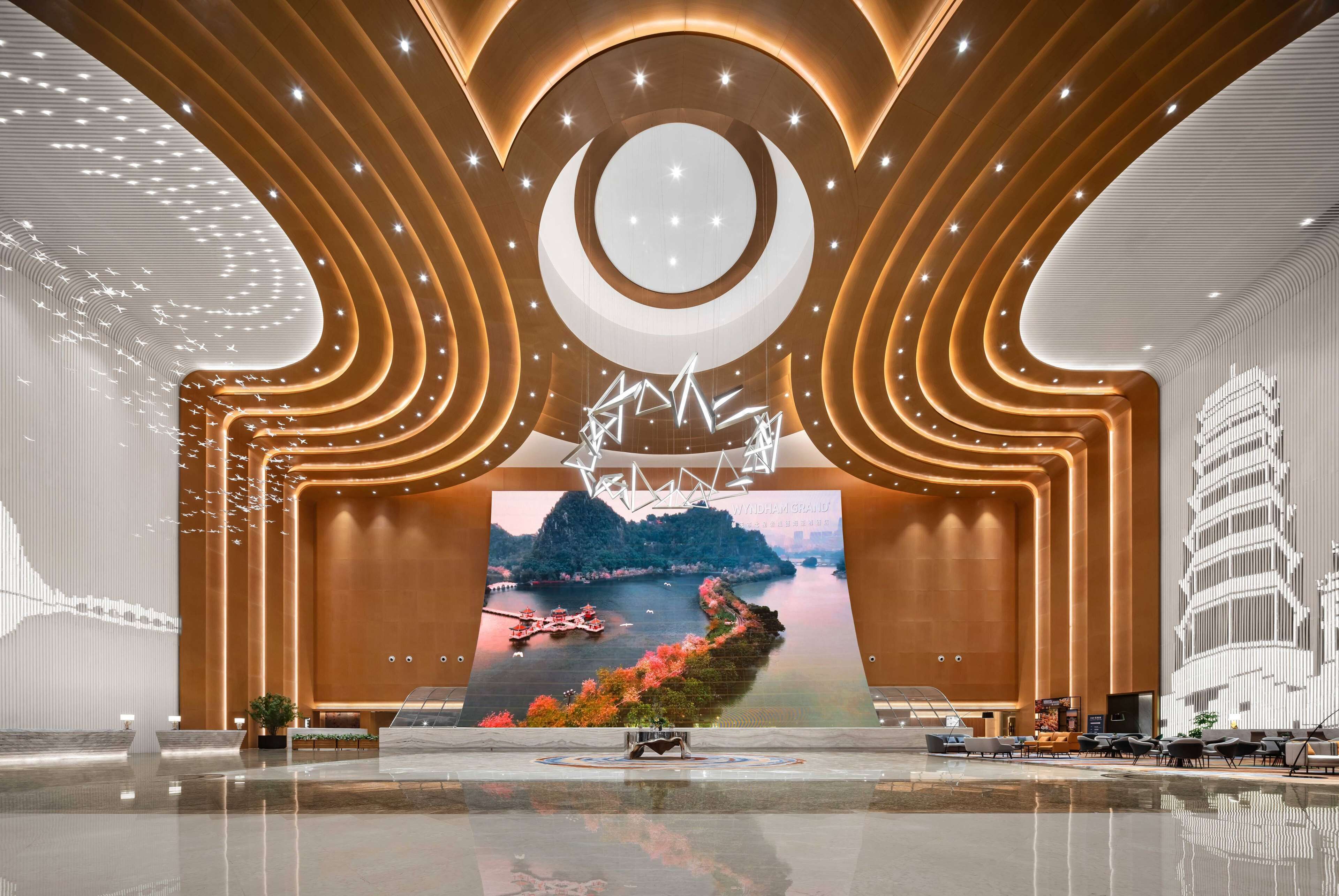 Um hall amplo com um grande painel digital, design de teto curvo e área de estar central.