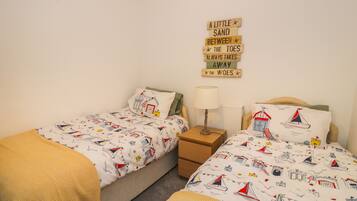 Quarto com duas camas de solteiro, cada uma com colcha de tema náutico, mesa de cabeceira com luminária e placa na parede com mensagem náutica.