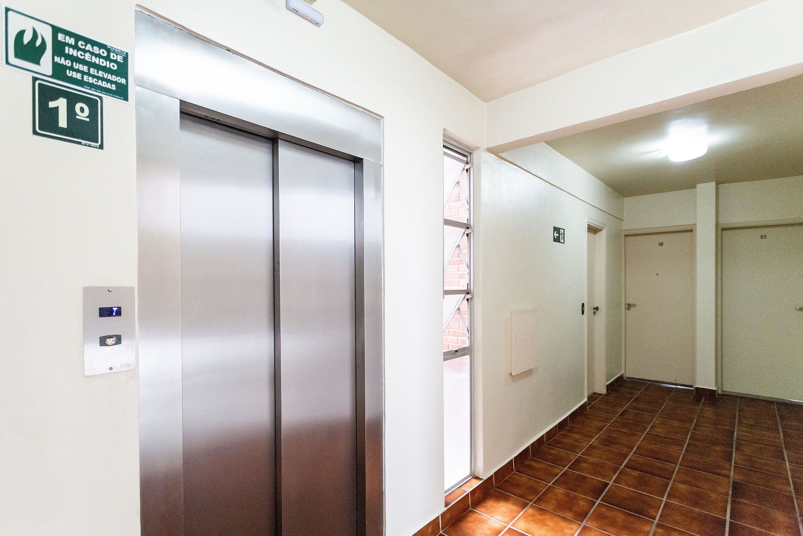 Um corredor com elevador, sinalização de saída de incêndio e uma porta numerada com o número 1.