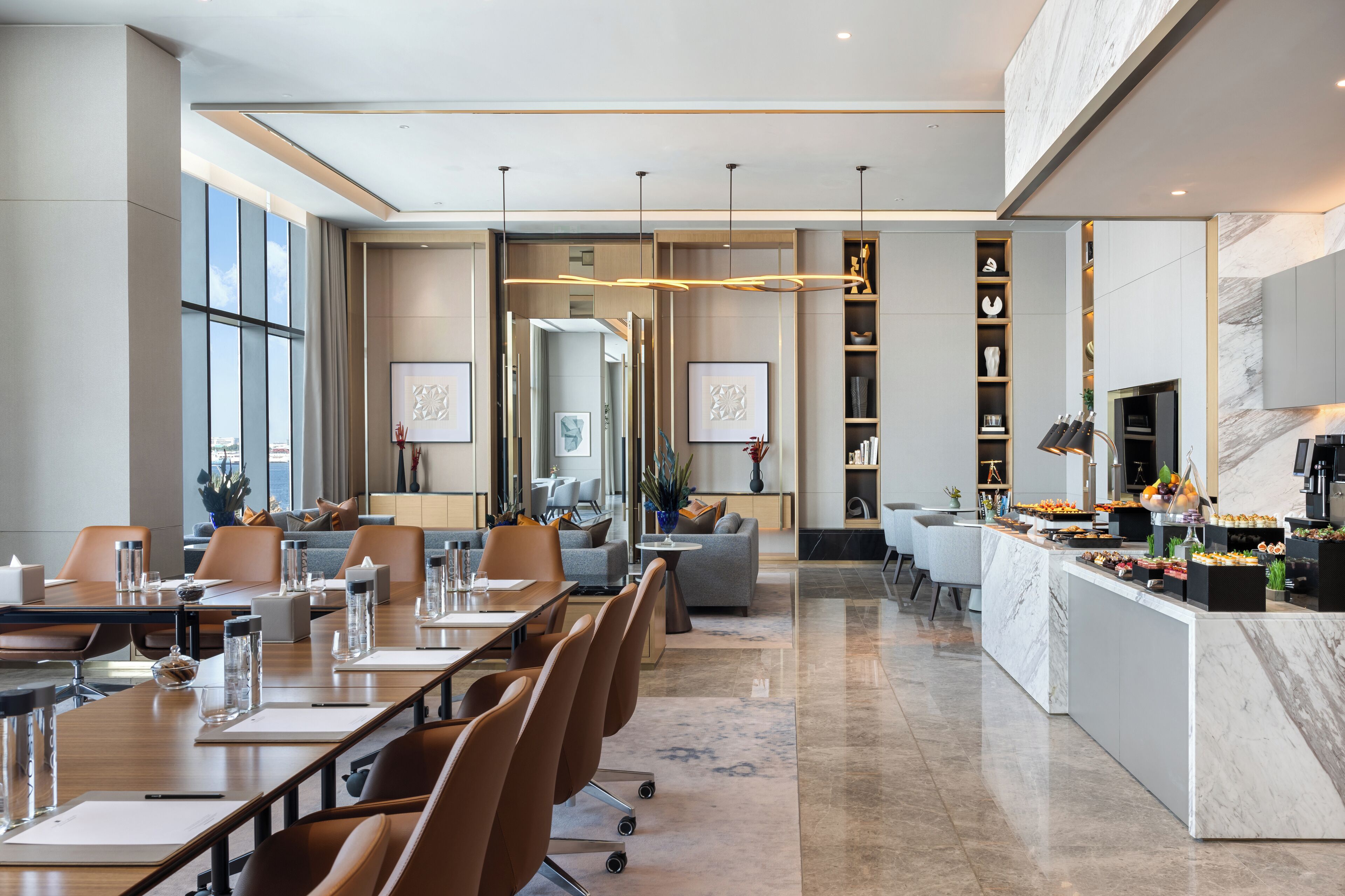 Uma sala de conferência moderna com uma mesa comprida, assentos confortáveis e uma área de cozinha com bancada de mármore.