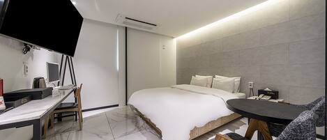 Quarto de hotel moderno com uma cama, uma escrivaninha com computador, uma cadeira e uma pequena mesa.