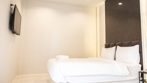 Quarto de hotel com uma cama grande, televisão de tela plana na parede e cabeceira escura.