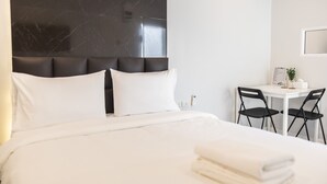 Quarto de hotel com uma cama grande, uma escrivaninha com duas cadeiras, uma mesinha de centro com uma planta e um espelho fixado na parede.