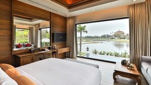 Quarto de hotel com uma cama grande, uma escrivaninha com televisão e vista para um lago e edifícios.