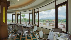 Restaurante com vista para a água e montanhas. Mesas montadas com pratos e copos.