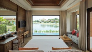 Quarto de hotel com uma cama grande, uma escrivaninha com televisão, um sofá e vista para um lago e edifícios.