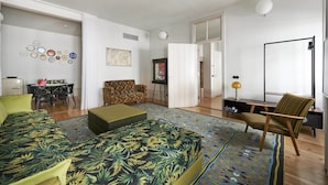 Uma sala ampla com uma cama grande, um sofá verde, um tapete estampado, uma cadeira de madeira e uma mesa de jantar com cadeiras.
