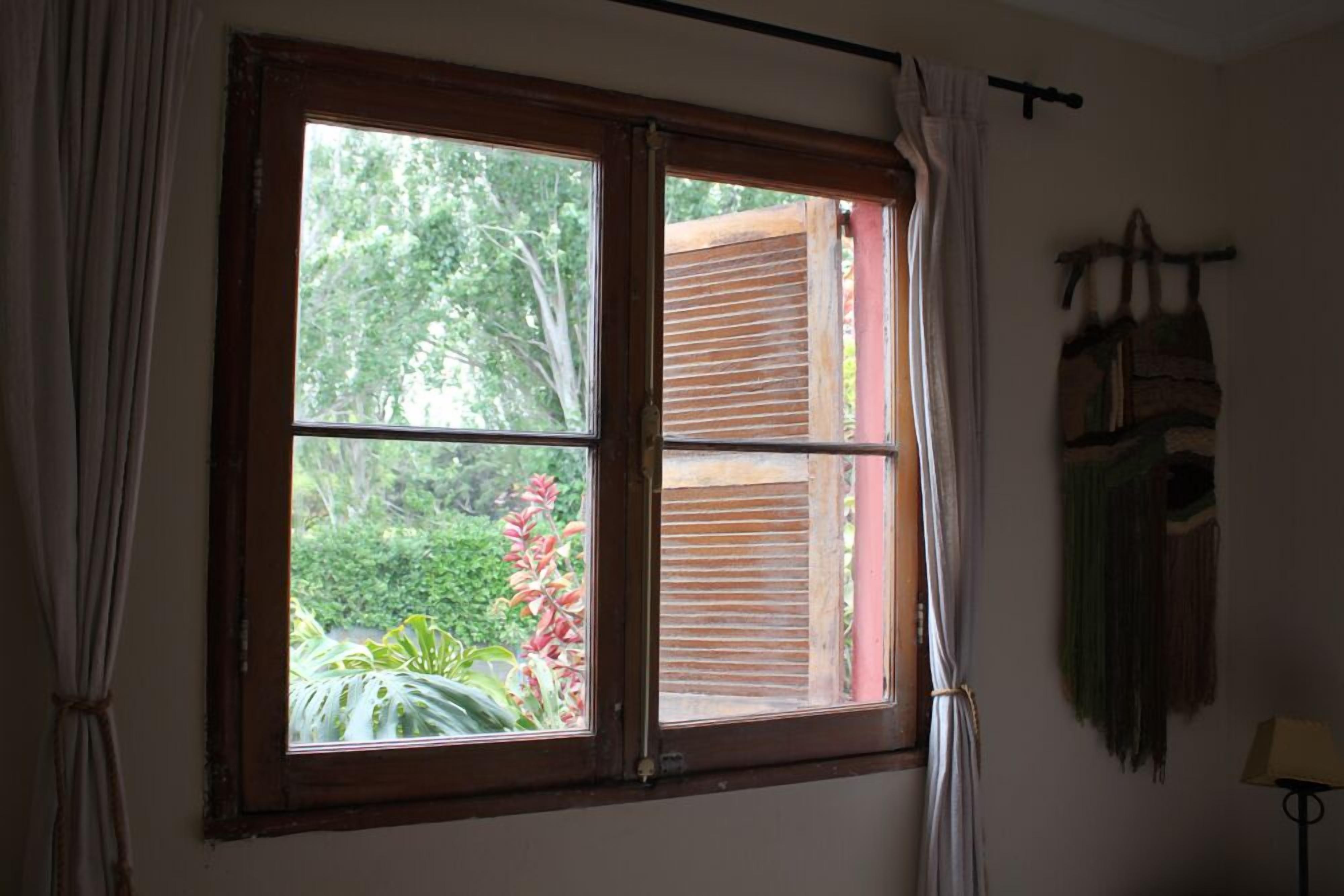 Um quarto com uma janela grande, cortinas e uma luminária fixada na parede.