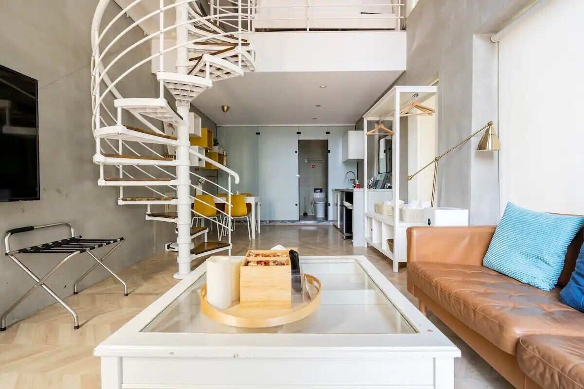 Uma sala de estar moderna com uma escada em espiral, uma mesa de centro de vidro, um sofá de couro e um lustre.