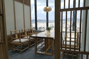Quarto com vista para a paisagem urbana, com uma mesa e cadeiras de madeira, luminária pendente e janela.