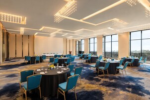Sala de conferências com mesas redondas, cadeiras azuis e piso coberto por carpete.