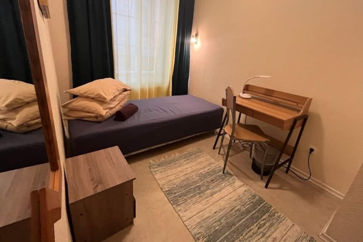 Um quarto pequeno e compacto com uma cama, uma escrivaninha e uma cadeira.