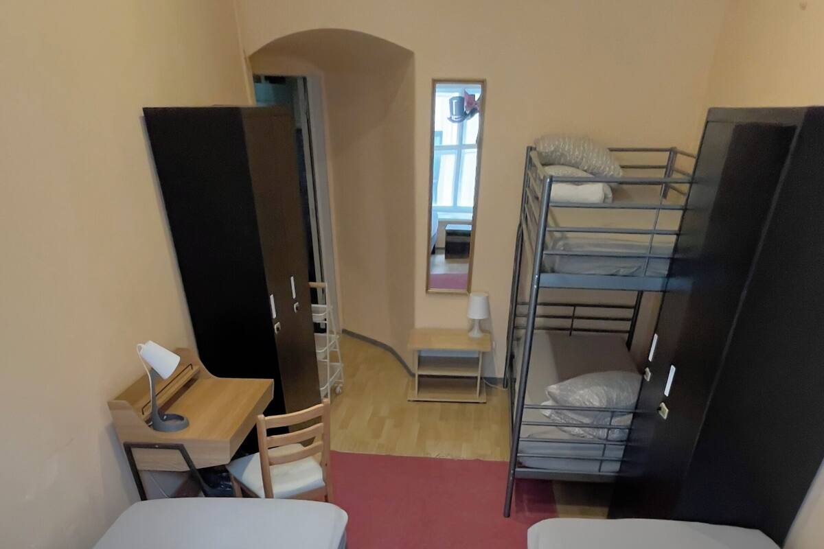 Quarto com duas camas, uma escrivaninha com luminária, um espelho e uma cama beliche.