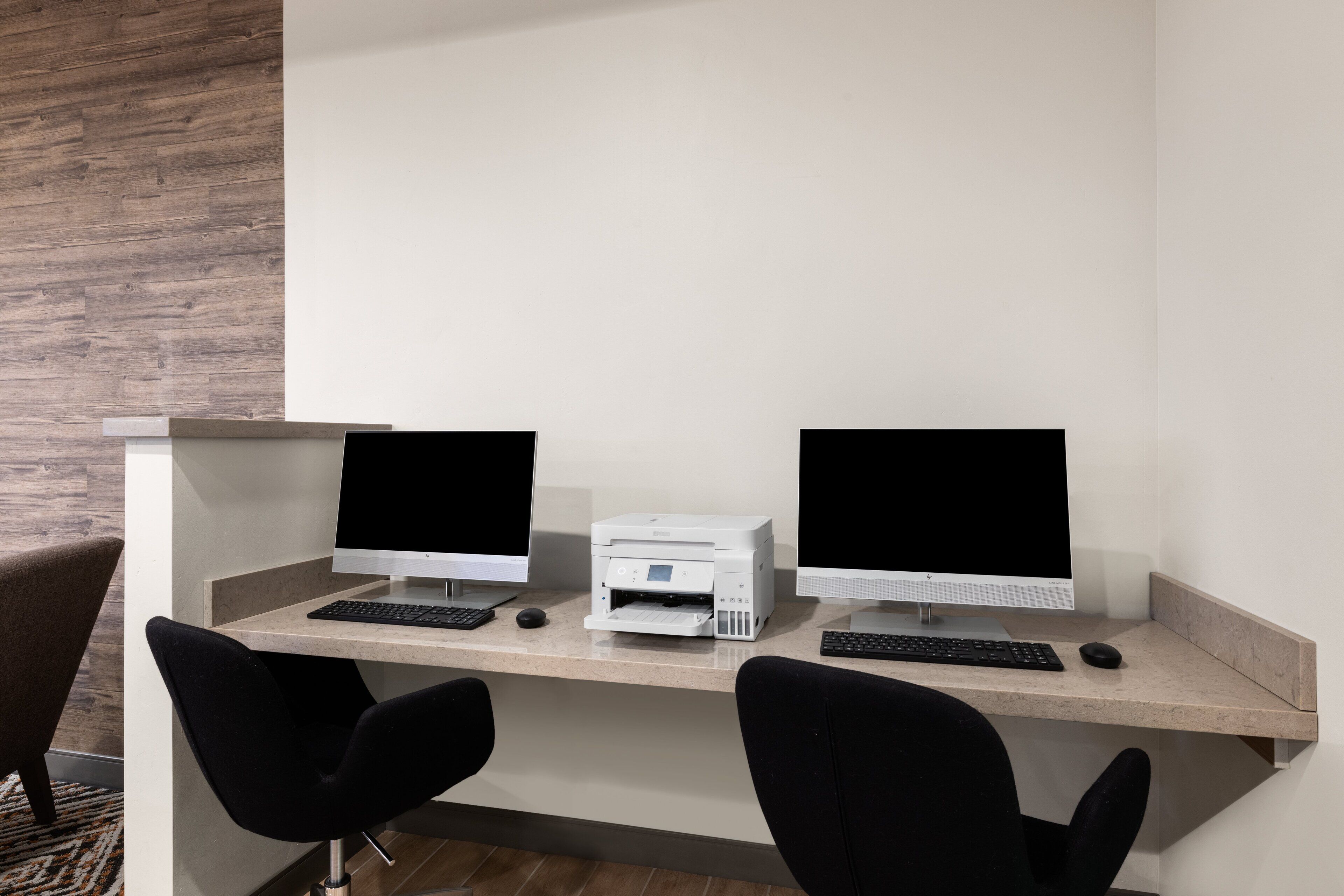 Um espaço de trabalho com dois monitores, uma impressora e duas cadeiras pretas.